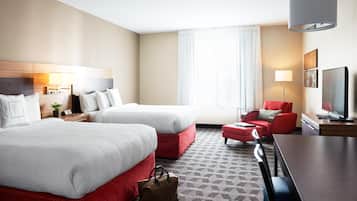 Quarto de hotel com duas camas, uma mesa, uma cadeira, uma televisão e uma janela com cortinas.