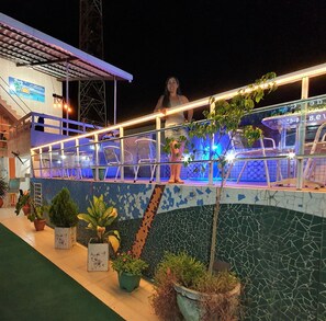 Um bar no terraço com guarda-corpo de vidro, plantas em vasos e uma parede revestida de azulejos.