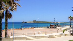 Um calçadão costeiro com vista clara para o mar, um pequeno edifício e uma ilha distante.