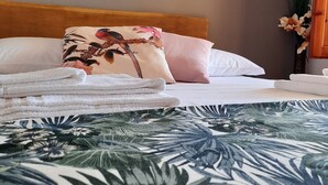 Uma cama bem arrumada com almofadas estampadas e lisas, cabeceira de madeira e edredom com padrão de folhagem tropical.