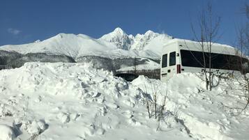 Paisagem coberta de neve com uma RV branca estacionada em uma encosta, cercada por neve e árvores.