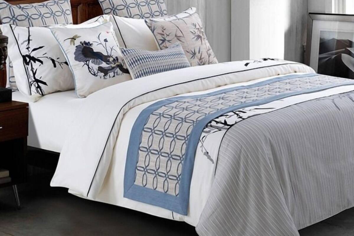 Cama bem arrumada com colcha estampada e almofadas combinando, cabeceira de madeira e mesa de cabeceira com abajur.