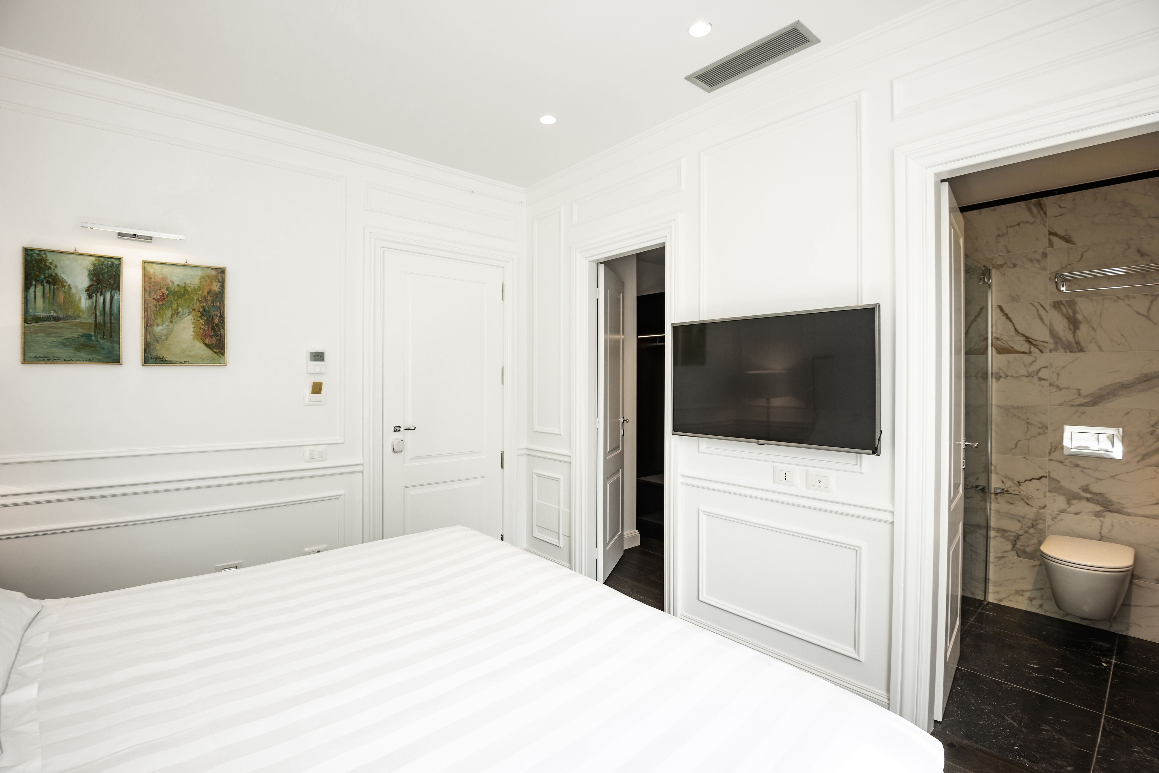 Quarto de hotel com uma cama grande, televisão fixada na parede e banheiro com chuveiro de mármore.