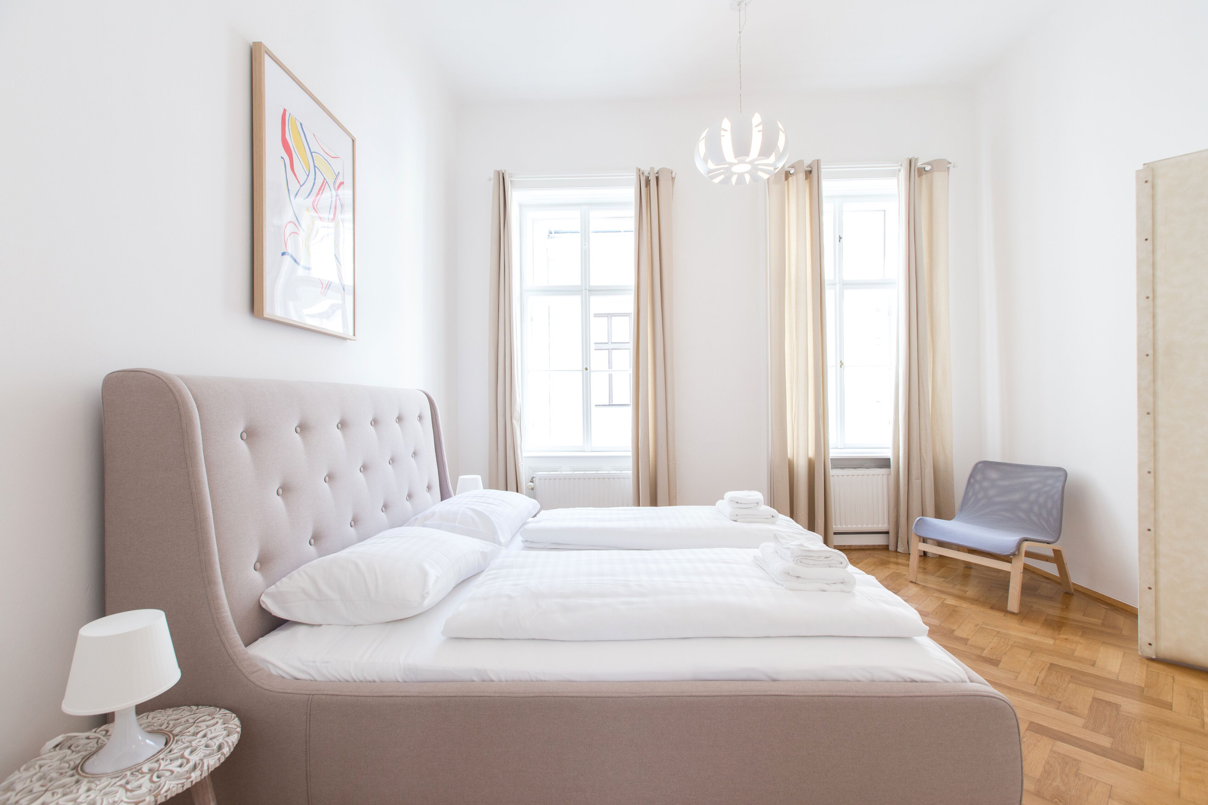 Quarto com cama grande, uma cadeira, mesa de cabeceira e janela com cortinas.