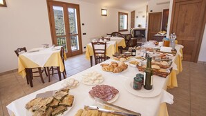 Espaço de refeições com várias mesas montadas para um buffet, com diversos tipos de comida e uma garrafa de azeite.