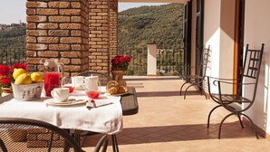 Uma varanda com mesa posta para o café da manhã, uma parede de tijolos e vista para uma paisagem montanhosa.