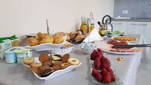 Mesa de buffet com diversos alimentos, incluindo doces, sanduíches e frutas frescas.