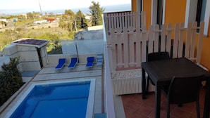 Área de piscina no terraço com mesa e cadeiras, cerca branca de piquete e vista do horizonte.