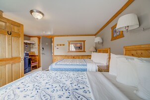 Quarto de hotel com duas camas, cabeceiras de madeira, luminária de teto e abajur na parede, além de um quadro emoldurado.