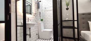 Um banheiro moderno com parede revestida de azulejos brancos, pia branca, vaso sanitário e chuveiro.