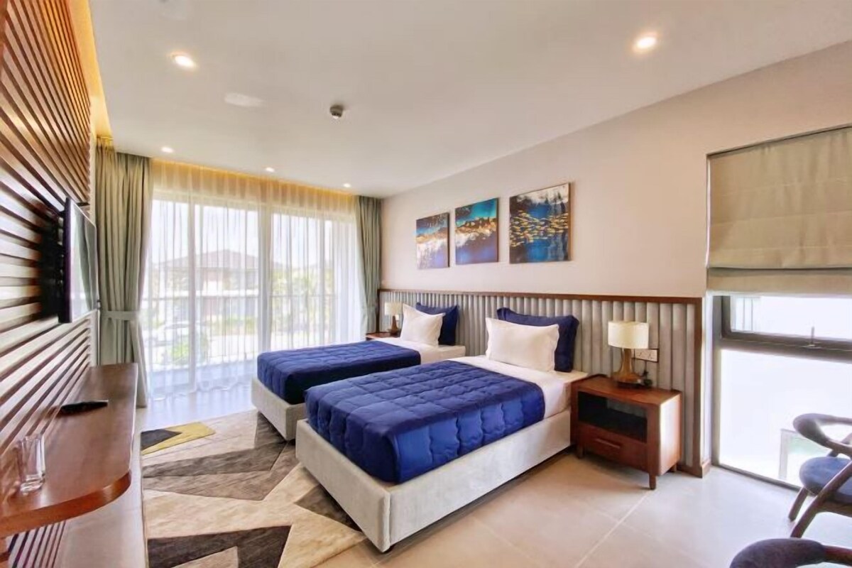 Quarto de hotel com duas camas, uma escrivaninha, uma cadeira, televisão e obras de arte na parede.
