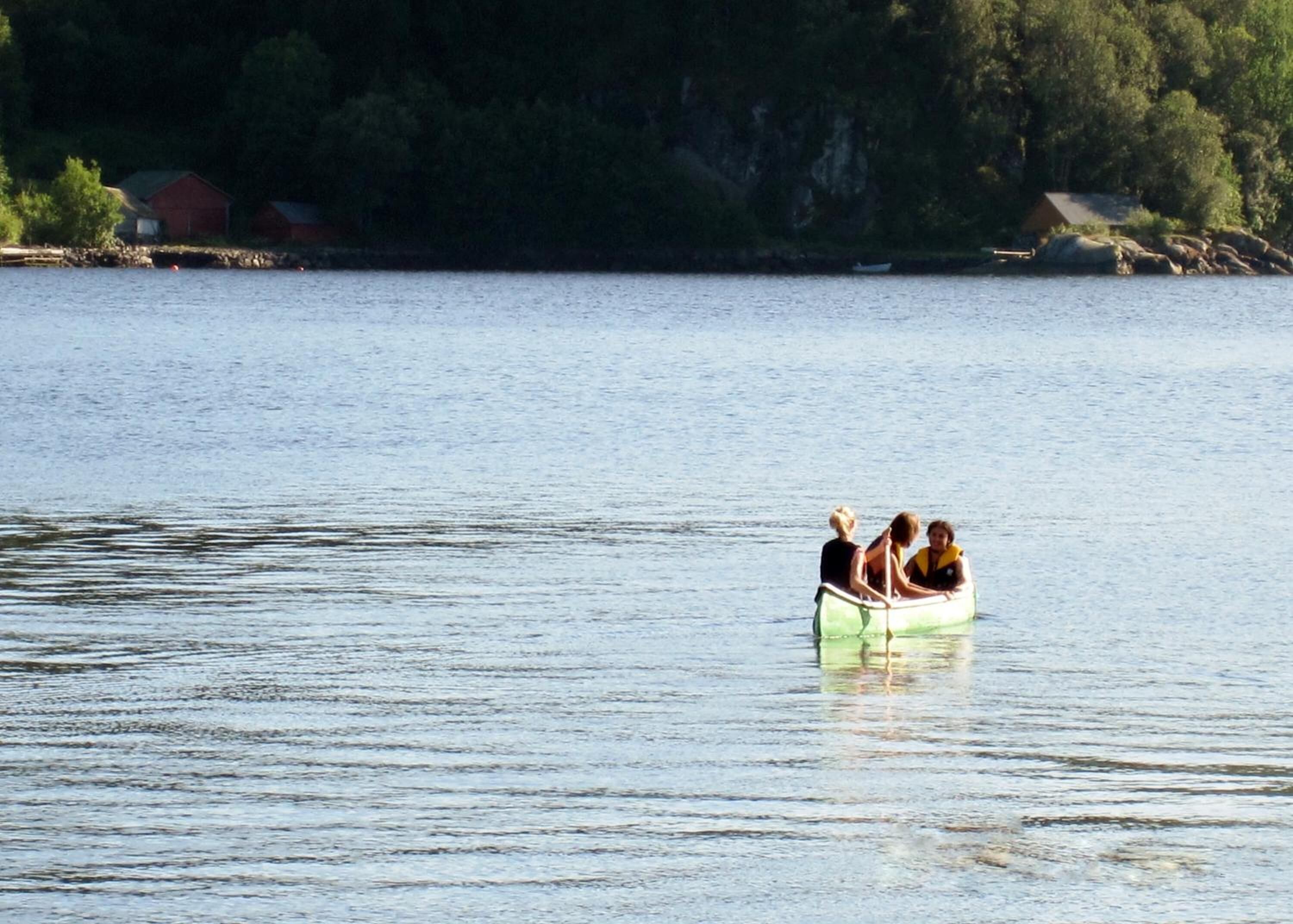 Um lago calmo com um barco canadense transportando três pessoas.