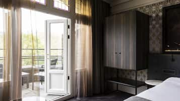 Quarto moderno com uma cama grande, uma pequena mesa de cabeceira, um guarda-roupa e uma porta de vidro deslizante para uma área externa com uma mesa e cadeiras.