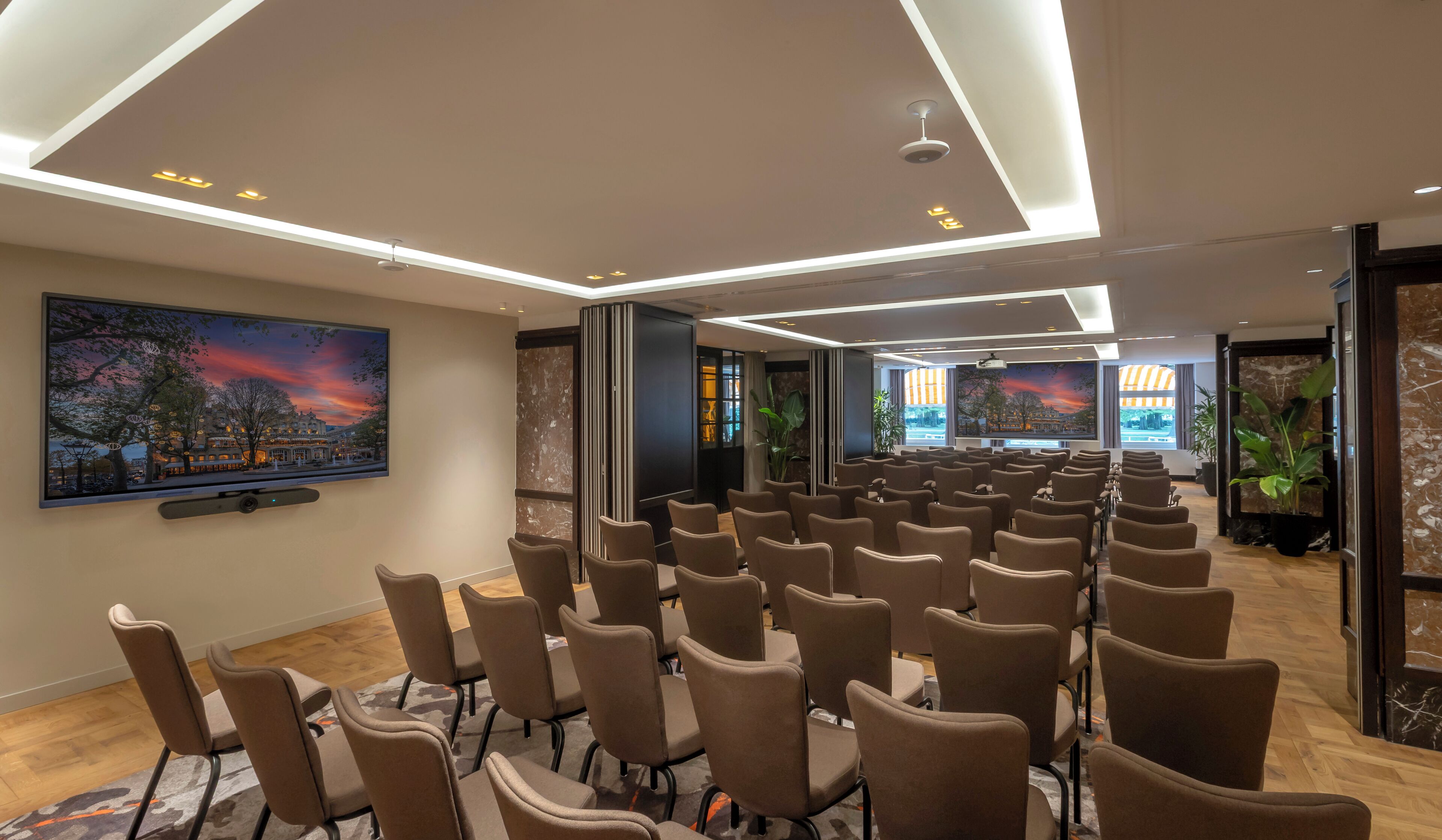 Uma sala de conferências com fileiras de cadeiras, uma grande pintura do pôr do sol e um design moderno no teto.