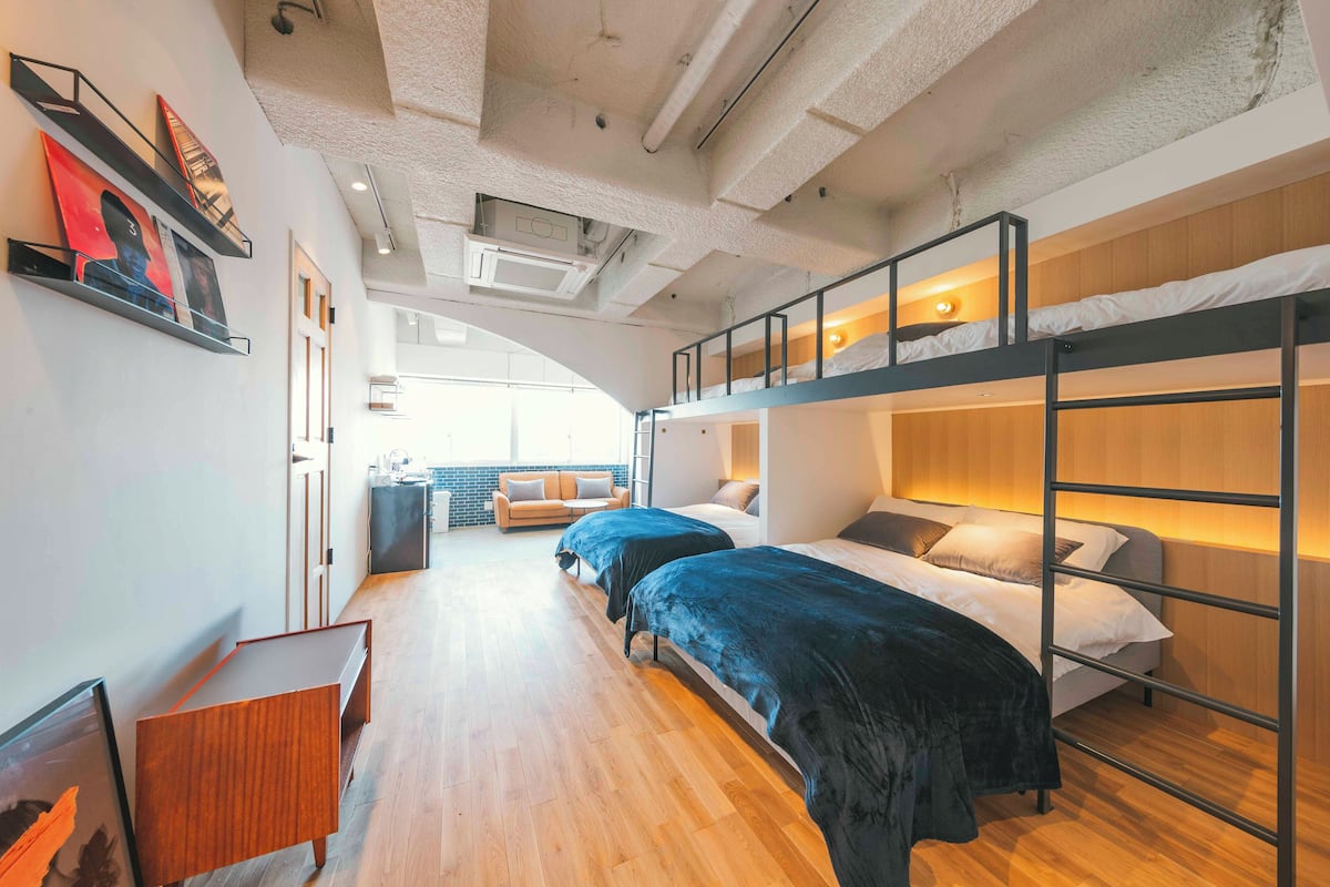 Quarto de hotel moderno com beliches, piso de madeira, sofá e escrivaninha.