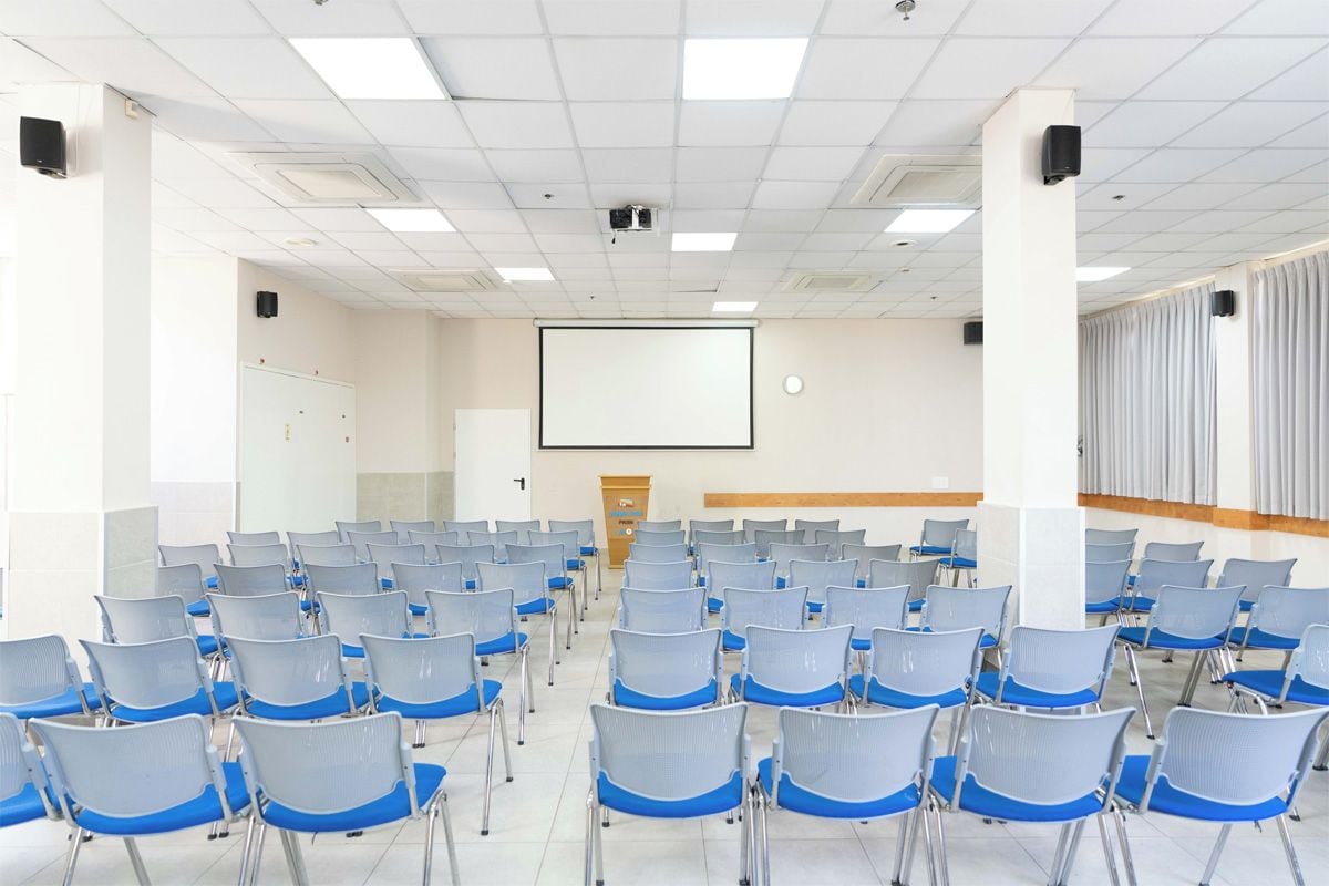 Uma sala de conferências com fileiras de cadeiras, uma tela de projetor e um pódio.