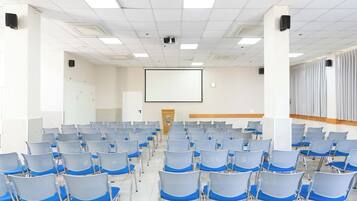Uma sala de conferências com fileiras de cadeiras, uma tela de projetor e um pódio.