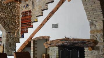 Um interior rústico com lareira de pedra, vigas de madeira e escadaria de pedra.