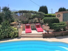 Piscina com cadeiras de sol vermelhas e uma parede de pedra.