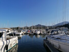 Marina com vários barcos atracados, águas calmas e montanhas ao fundo.