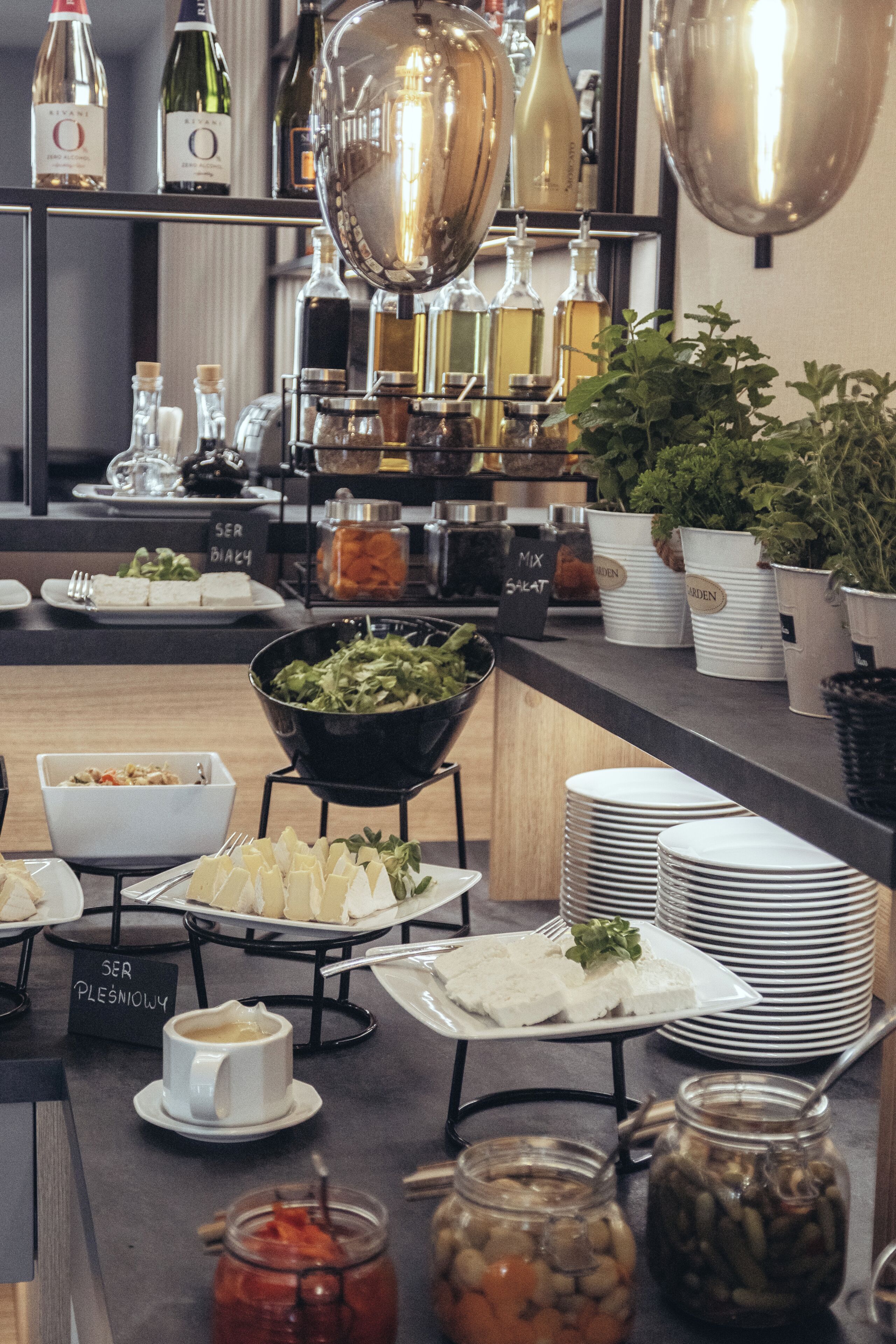Disposição de buffet com diversos alimentos e acompanhamentos, incluindo saladas, queijos e potes de picles.