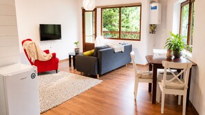 Uma sala de estar moderna com sofá, uma poltrona vermelha, televisão, mesa de jantar e um vaso de planta.
