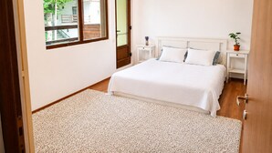 Quarto com cama, mesa de cabeceira, planta em vaso e janela.