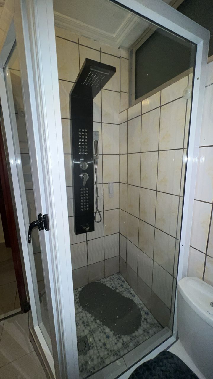 Chuveiro com painel de controle, paredes revestidas de azulejo e porta de vidro.