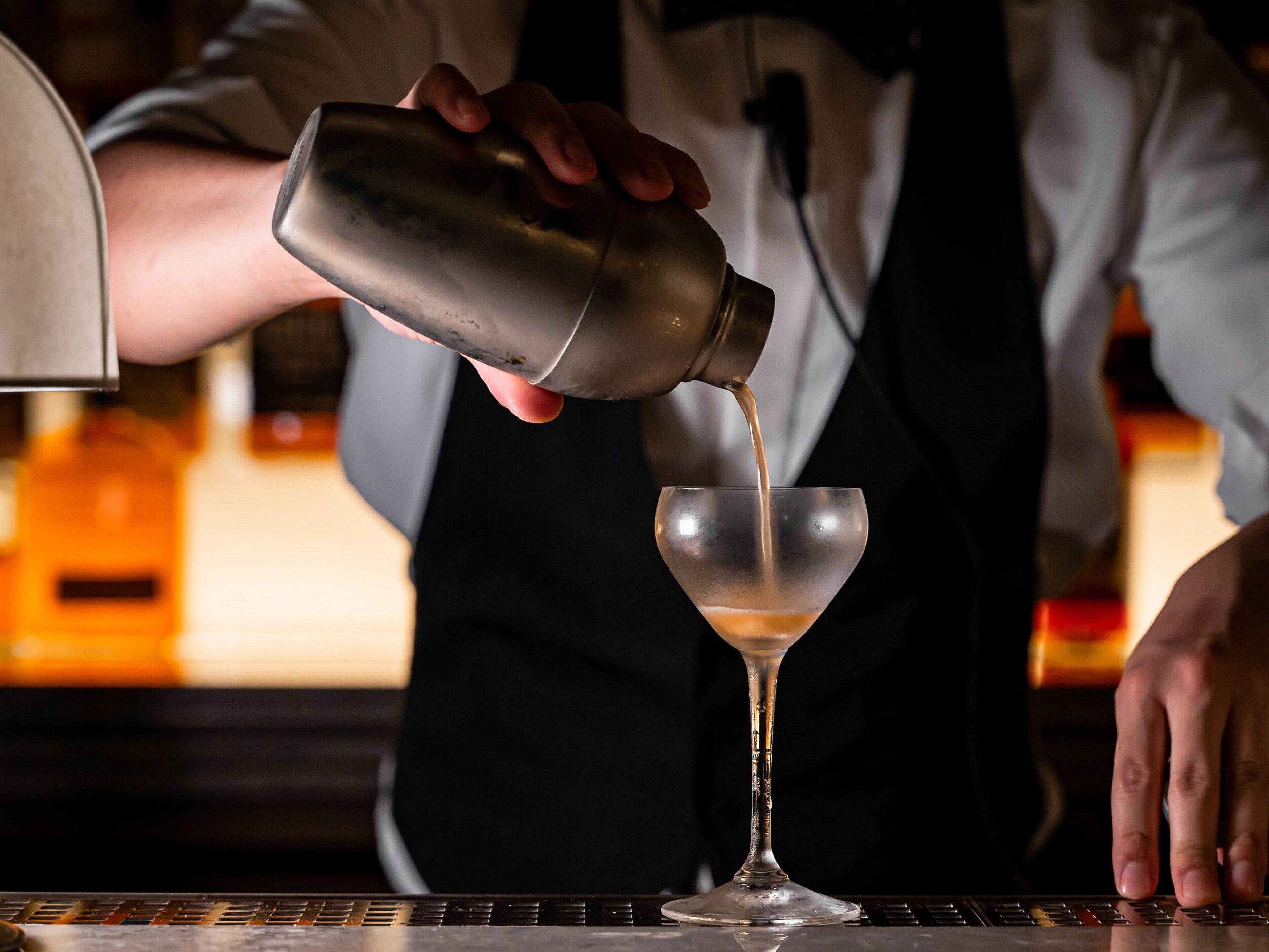 Um bartender a servir uma bebida num copo de martini.