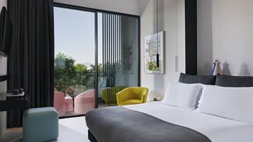 Quarto de hotel moderno com uma cama grande, uma escrivaninha, uma cadeira e uma varanda com vista para o verde.