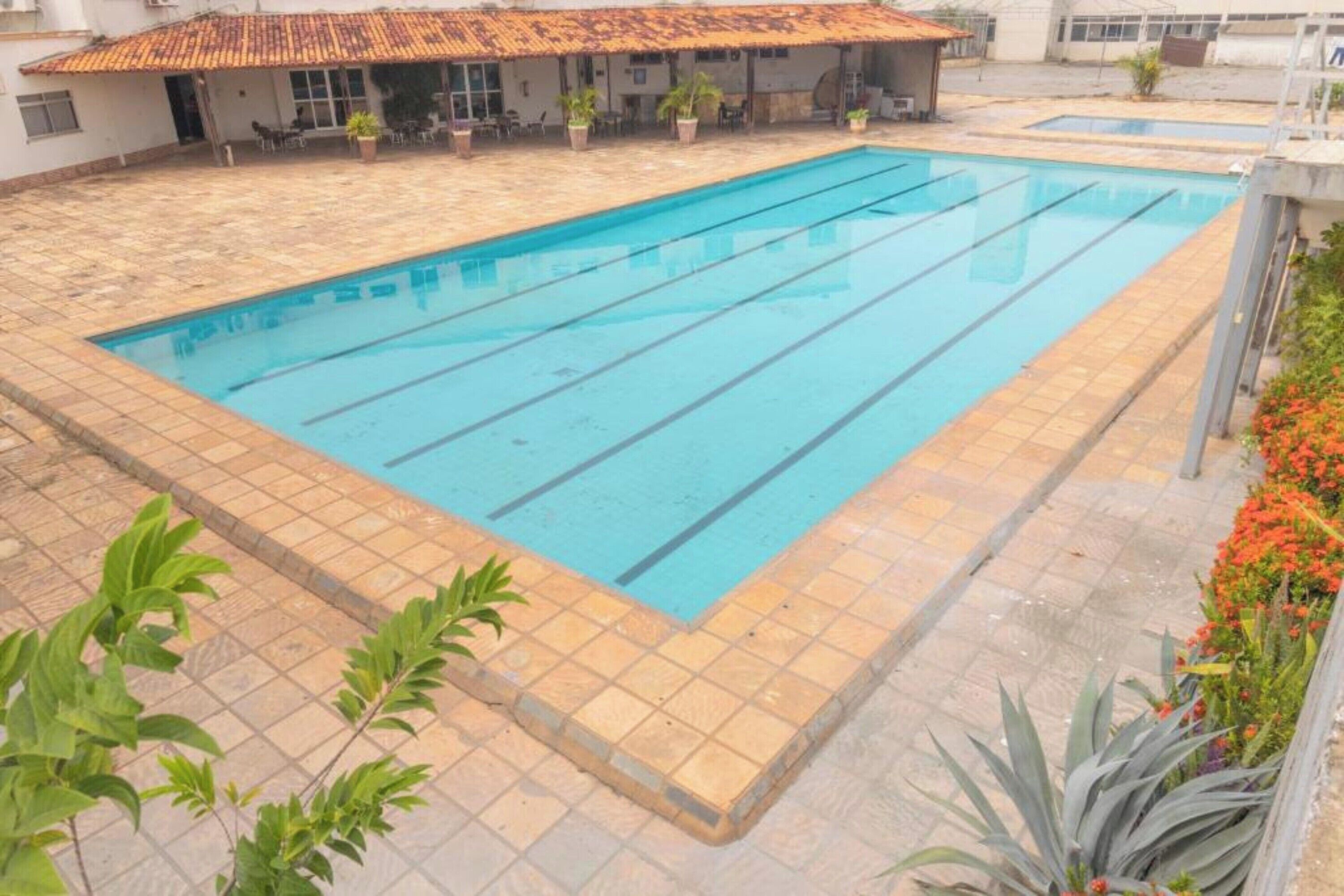 Piscina retangular com água azul cristalina, rodeada por um deck ladrilhado.