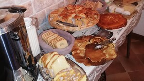Uma mesa de buffet com diversos produtos de pastelaria, uma máquina de café e uma chaleira.