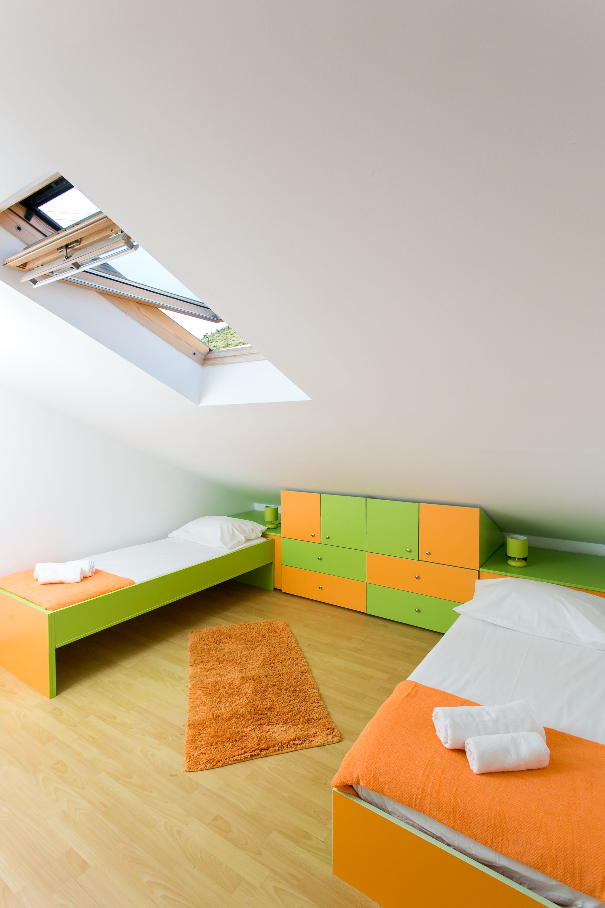 Quarto com duas camas, um claraboia e um penteou de cor verde e laranja.