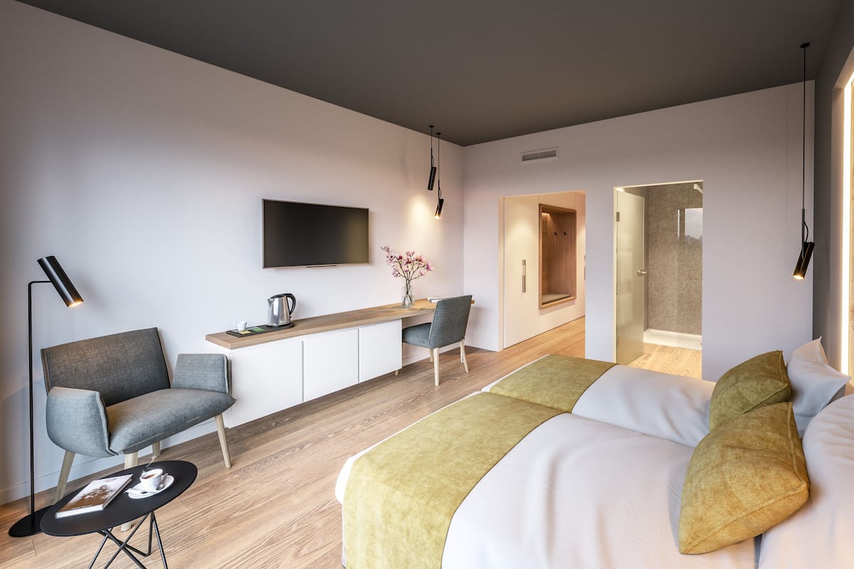Quarto de hotel moderno com cama, escrivaninha, cadeira, mesa de centro e televisão.