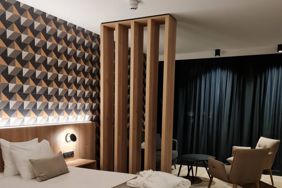 Quarto de hotel moderno com uma cama grande, um painel de madeira, uma escrivaninha, uma cadeira e vista para a cidade.