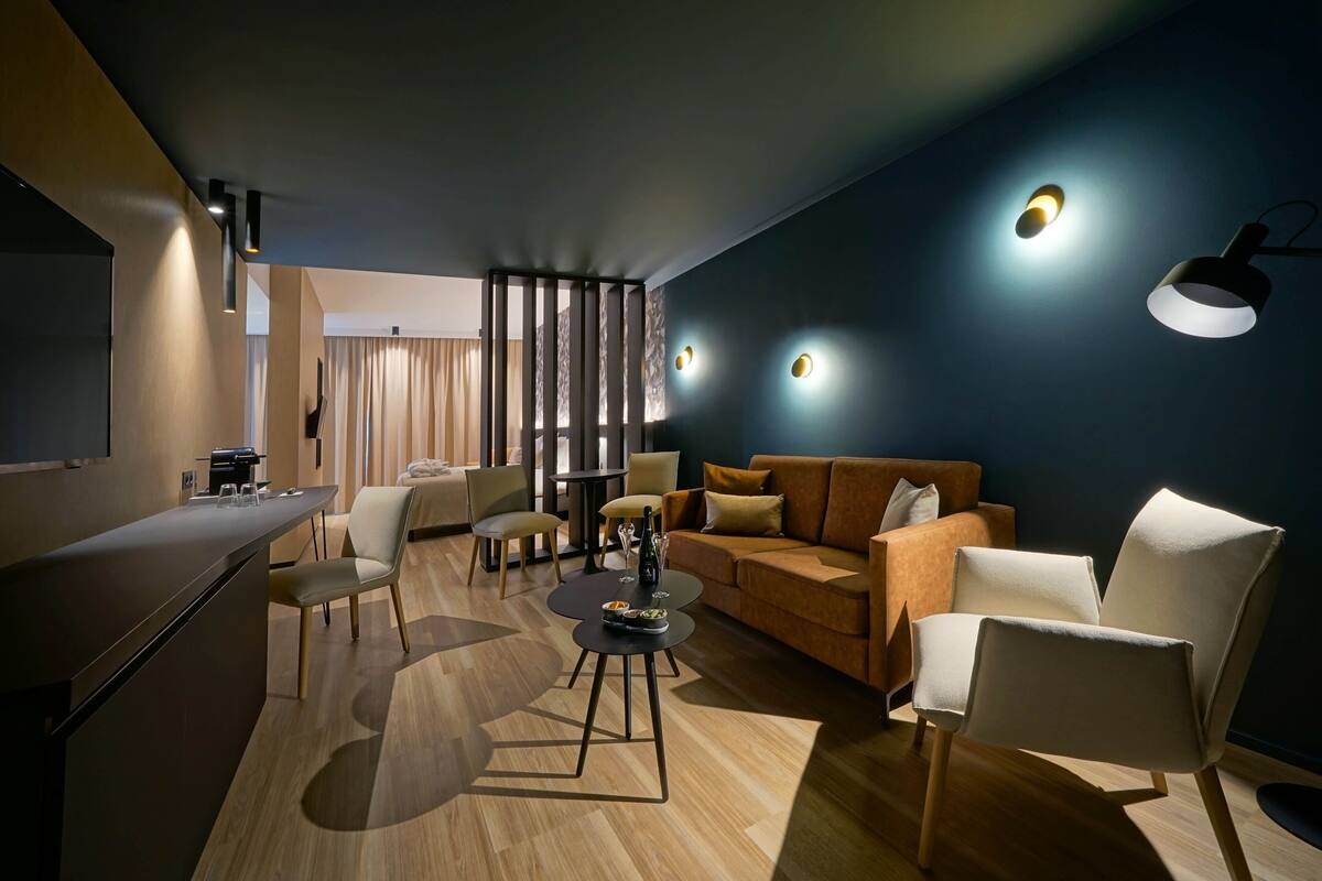 Uma sala de estar moderna com sofá, cadeiras, mesa de centro e área de cozinha com bancada e eletrodomésticos.