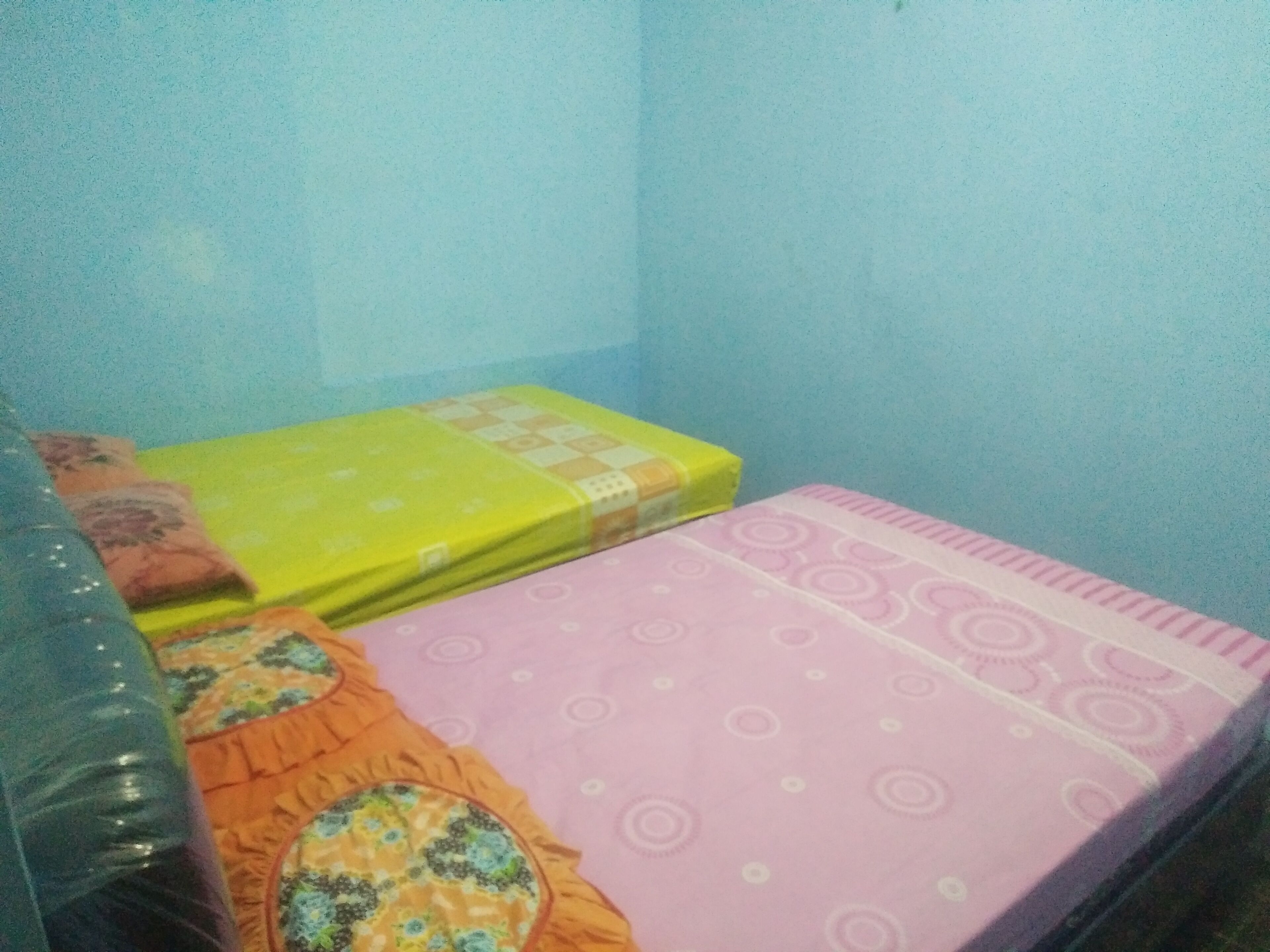 Quarto pequeno com duas camas, uma com colcha amarela e outra com colcha rosa.