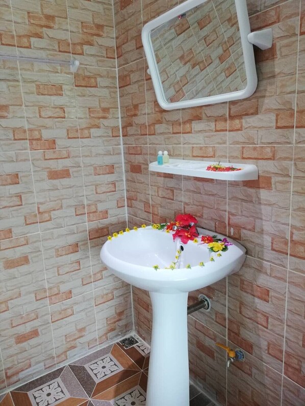 Um banheiro com pia de pedestal branca, um espelho acima e uma prateleira com produtos de higiene pessoal.