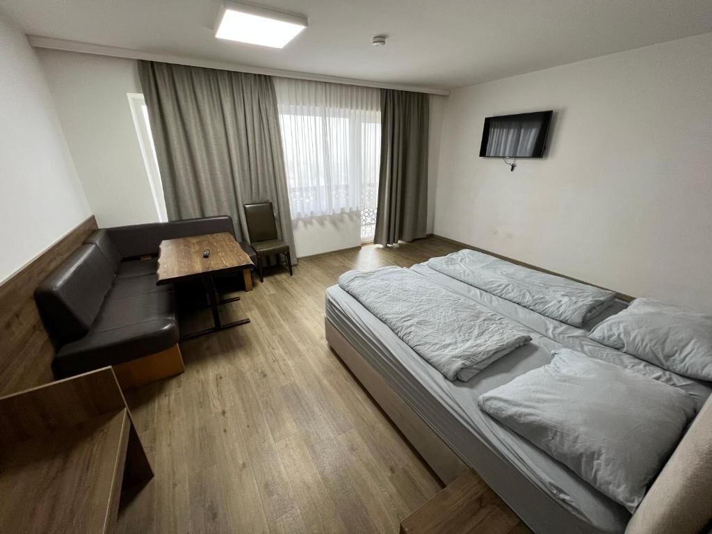 Quarto de hotel com sofá, mesa pequena, televisão e cama.