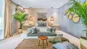 Um quarto moderno com cama, mesas de cabeceira, mesa de centro e elementos decorativos como quadros e plantas.