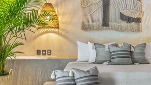 Quarto moderno com cama grande, tapeçaria na parede, planta em vaso e pequena mesa de madeira.