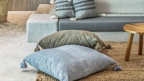 Quarto moderno com cama, almofadas, mesa de cabeceira, abajur e planta em vaso.