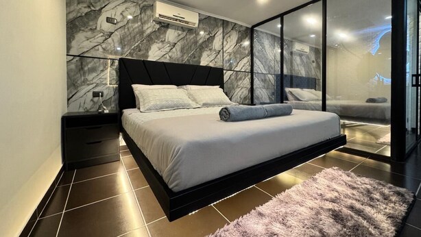 Quarto moderno com cama suspensa, parede de mármore e divisória de vidro.