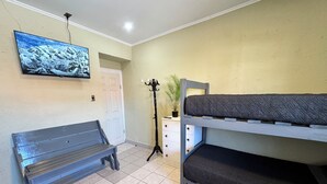 Um quarto com beliche, um banco, uma planta em vaso e uma televisão na parede.