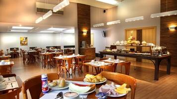 Espaço de refeições de hotel com várias mesas, cadeiras e um buffet.
