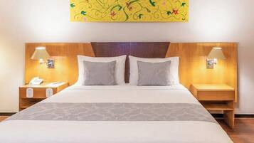 Quarto de hotel com uma cama grande, duas mesas de cabeceira, uma luminária de parede e um quadro decorativo.