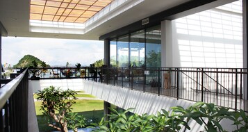 Um edifício moderno com fachada de vidro, área externa coberta com assentos e vista para uma colina.