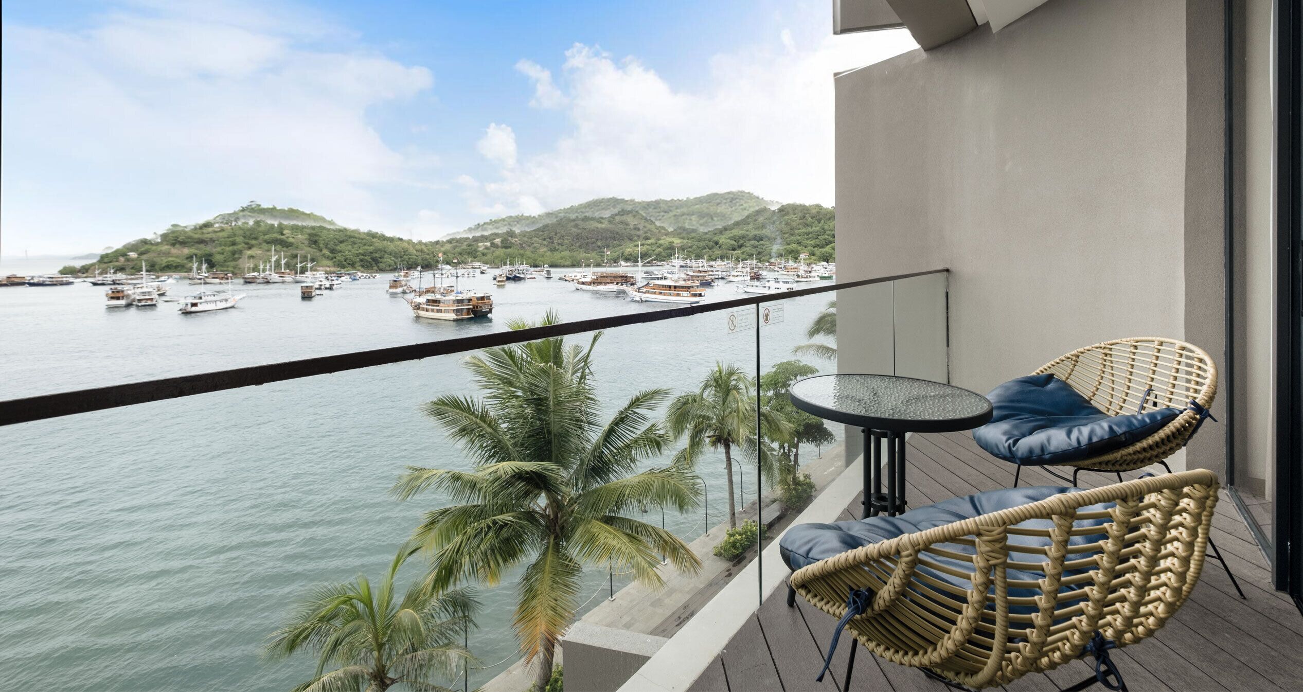 Varanda com cadeiras de vime, uma pequena mesa e vista para barcos e colinas.