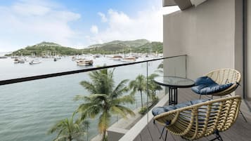 Varanda com cadeiras de vime, uma pequena mesa e vista para barcos e colinas.
