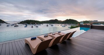 Terraço com espreguiçadeiras com vista para uma marina, barcos e a costa.